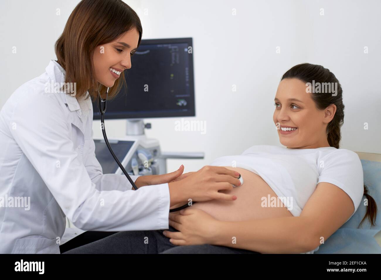 Professional gynecologist using stethoscope for examining tummy of ...