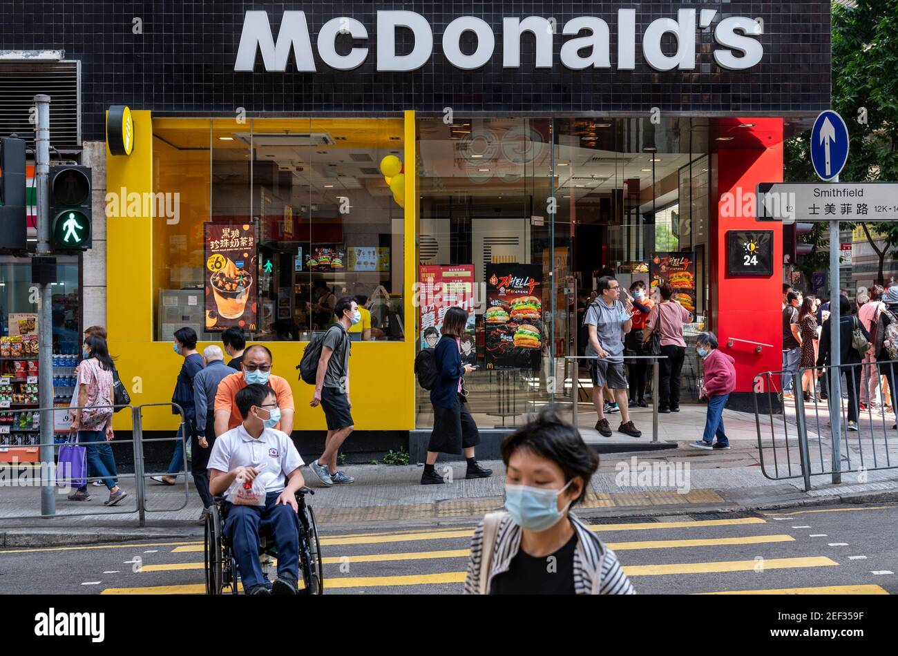 Pedestrians wearing face masks cross the street at a traffic light in ...