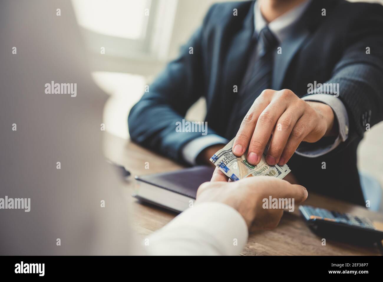 Businessman giving money, US dollars, to his partner in the office ...