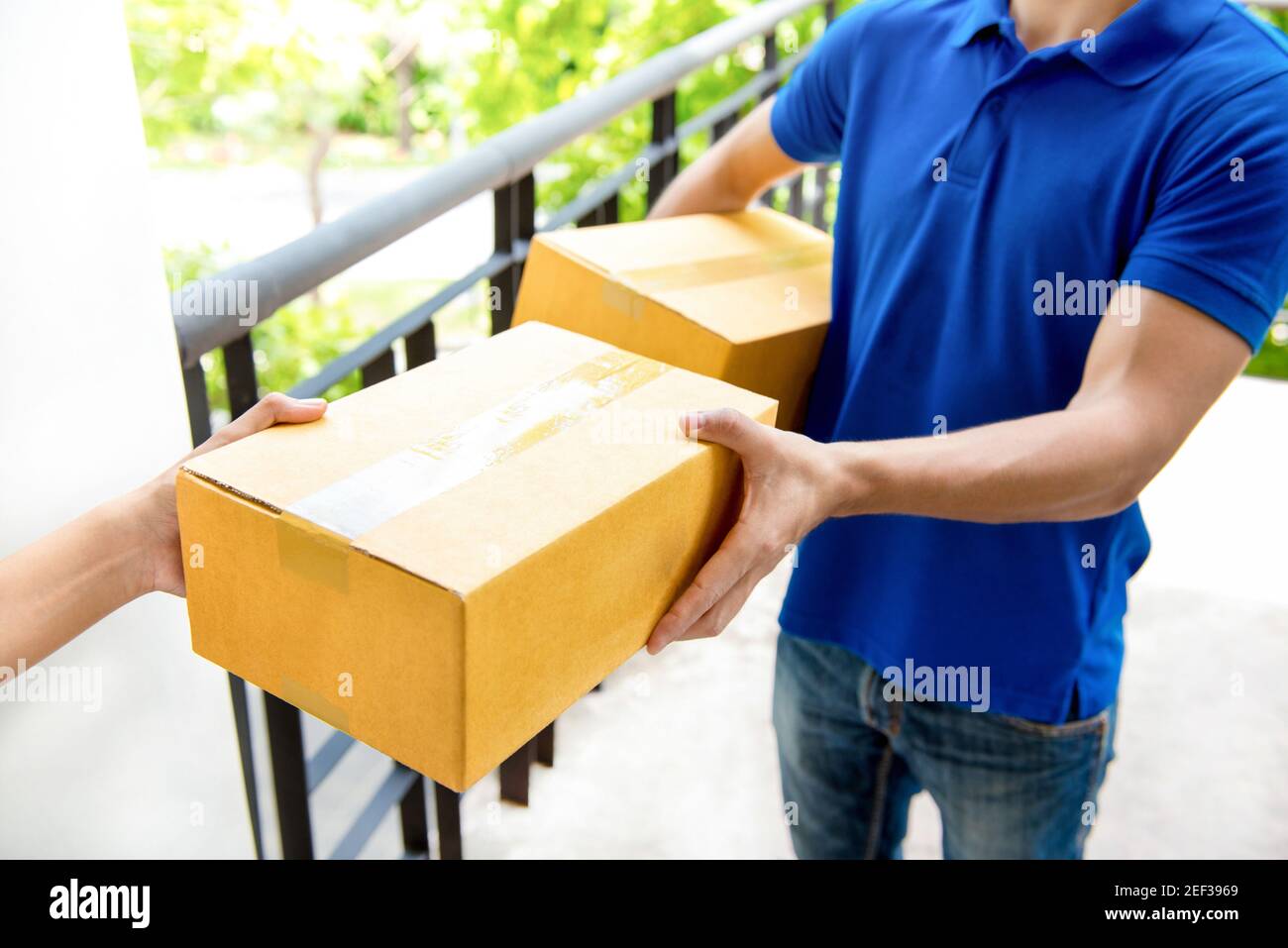 Delivery man in blue uniform handing parcel box to recipient - courier ...