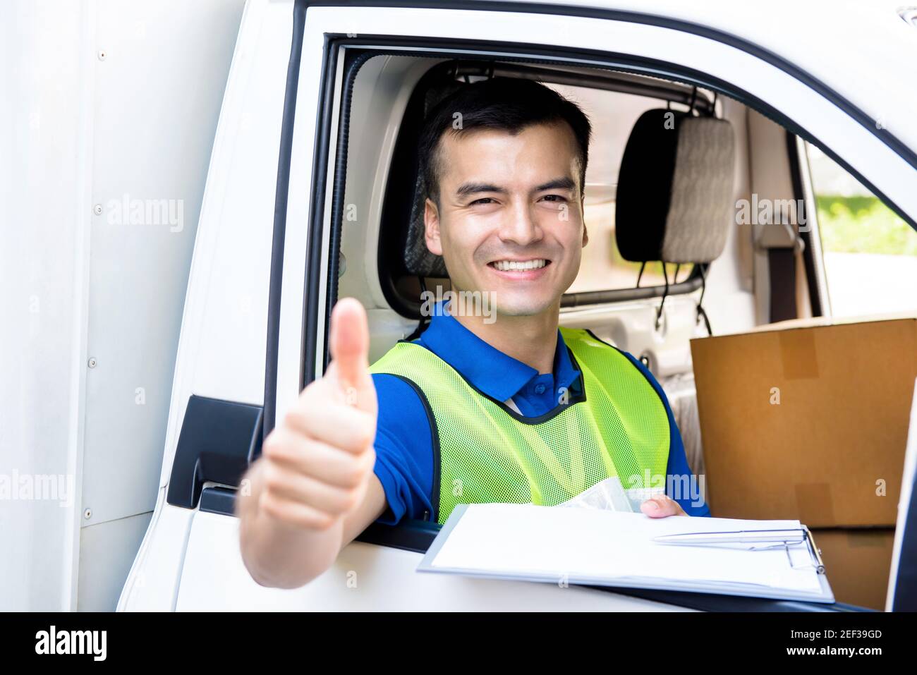 Smiling delivery man sitting in the car as a driver, giving thumbs up ...
