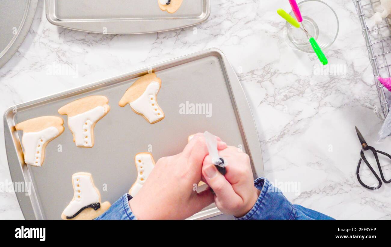 Flat lay. Decorating ice skate shaped sugar cookies with black color ...