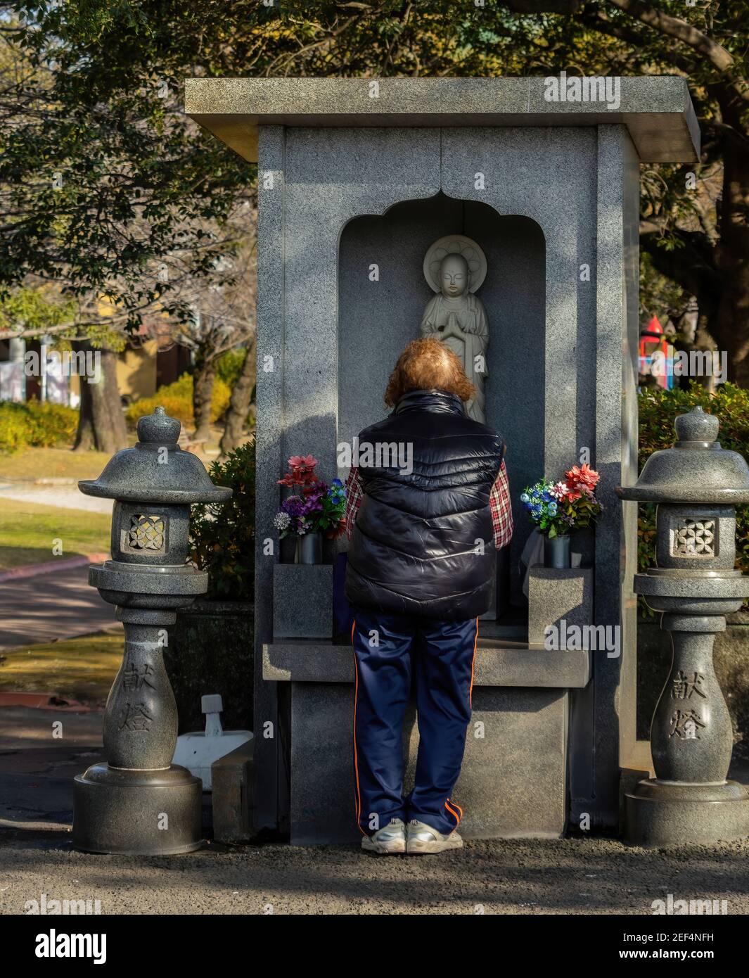 An old lady prays at an outdoor, Buddhist mini shrine for the well ...