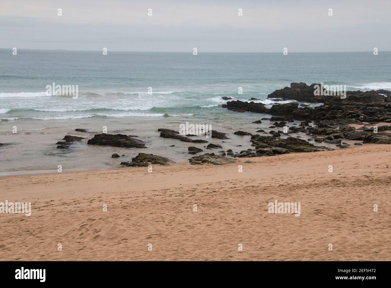 Waves breaking in the shallows into black rocks on shoreline Stock ...