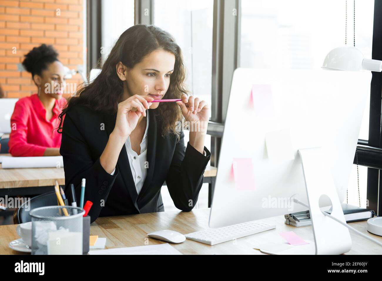 Business woman holding pencil while concentrating on computer screen at ...