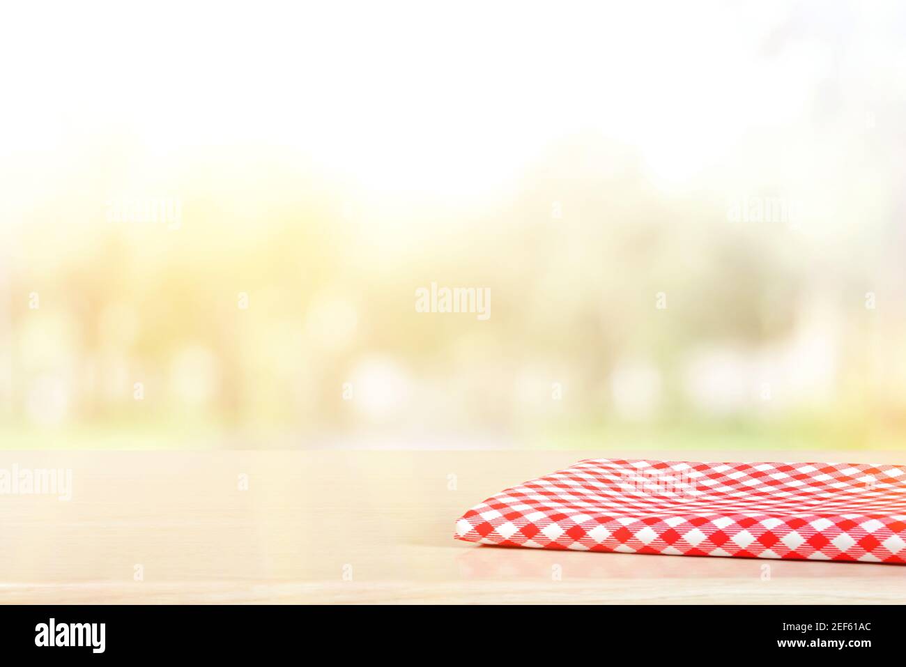 Red checkered cloth on wood table top in blur green background of trees ...