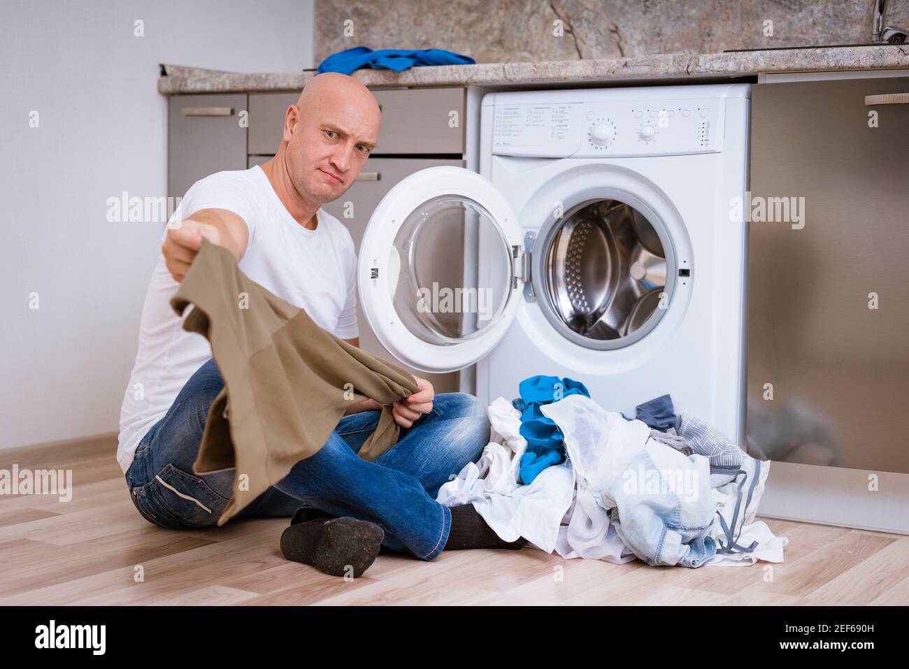 tired bald man sitting with dirty laundry in the washing machine ...