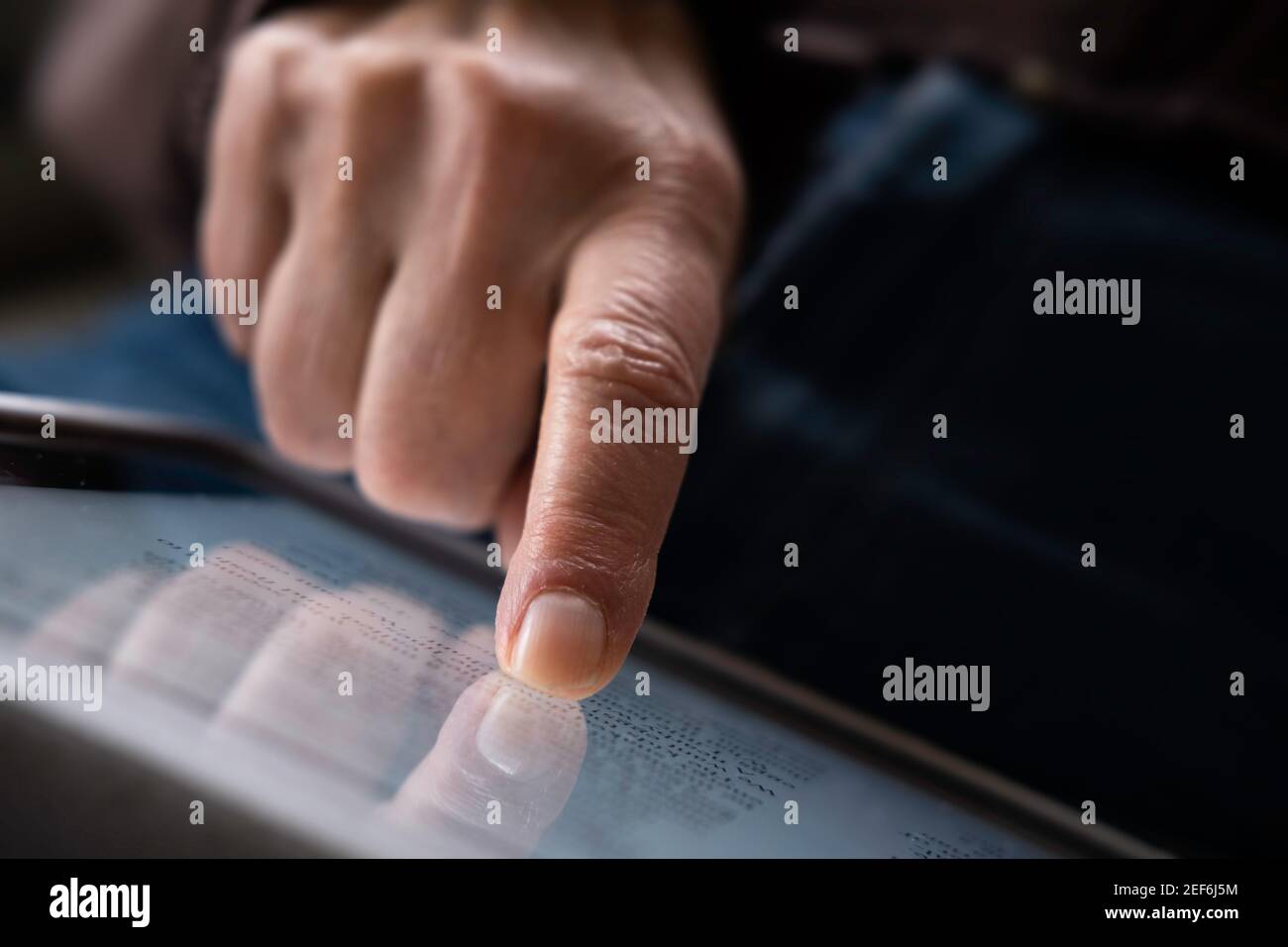 Close-up of finger and hand on the touchscreen of a tablet with dark ...