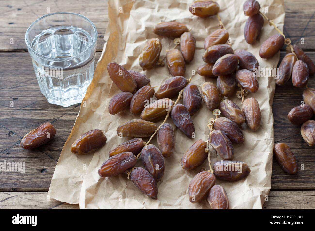 Dried dates fruits on a branch and a glass of water on a wooden table ...