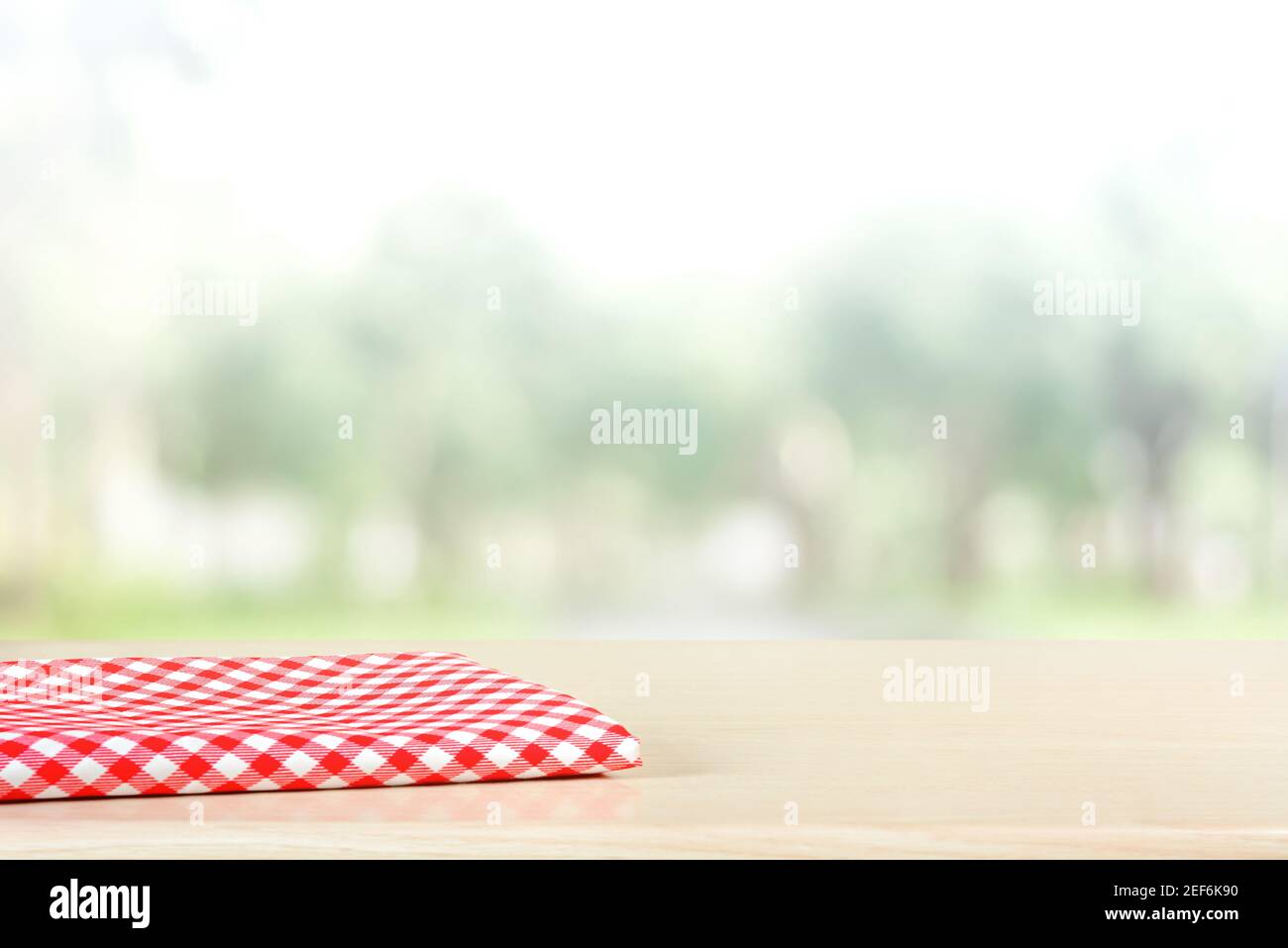 Red checkered cloth on wood table top in blur green background of trees ...