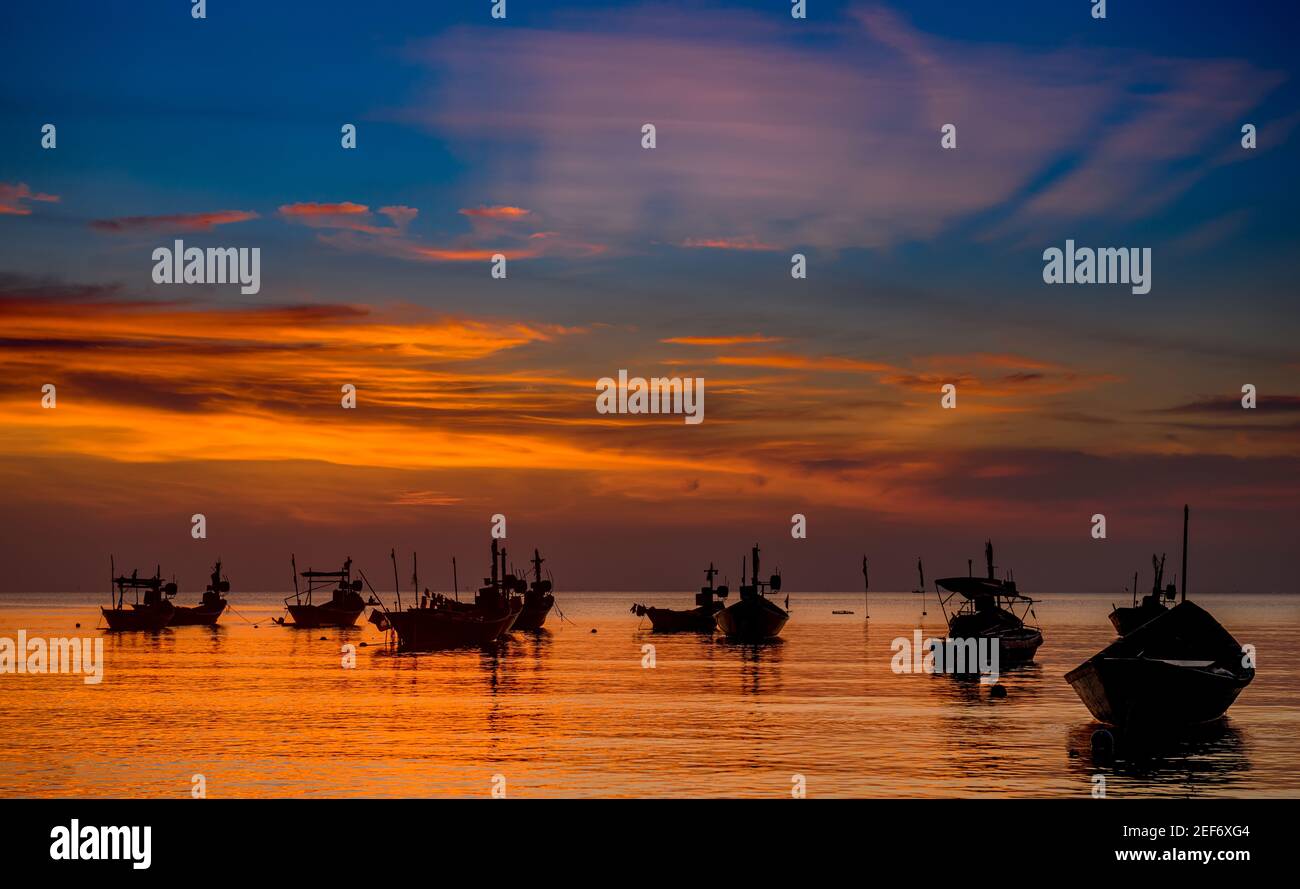 Silhouette fishery boats in the sea with sunset warm low lighting and ...
