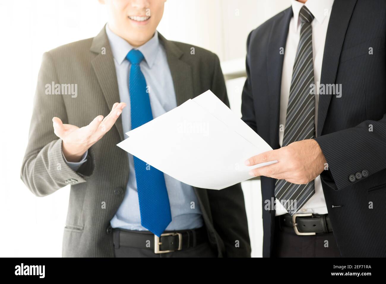 Two businessmen standing together discussing document Stock Photo - Alamy