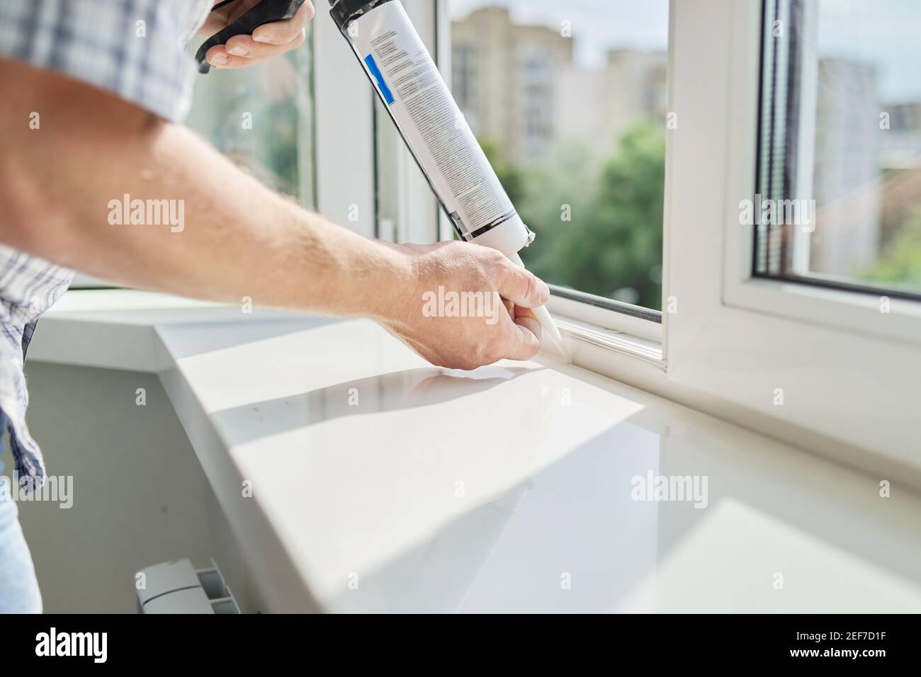 A worker with a construction syringe fills seam between sill and window with silicone sealant ...