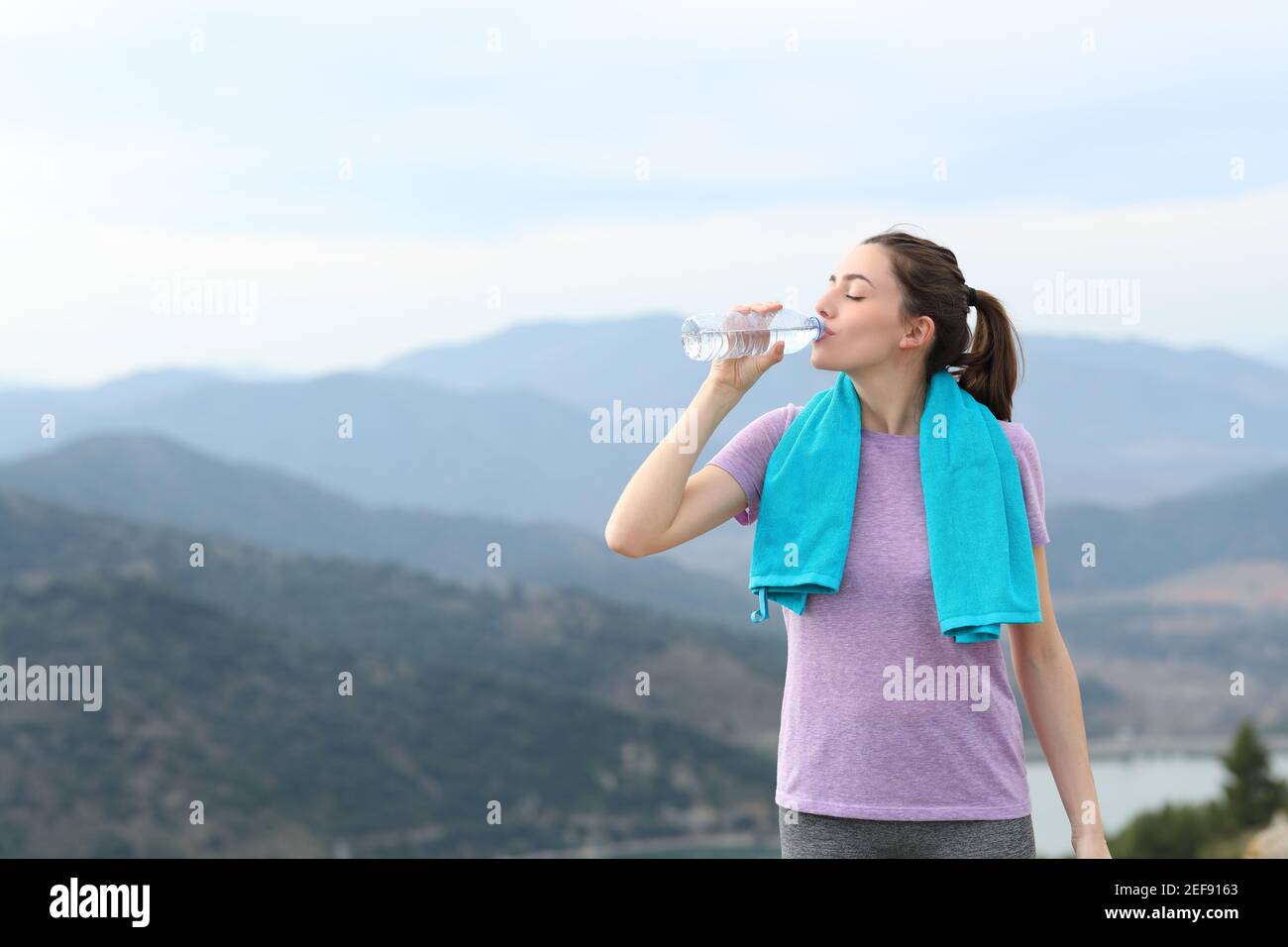 Happy runner drinking water from plastic bottle after sport in the ...