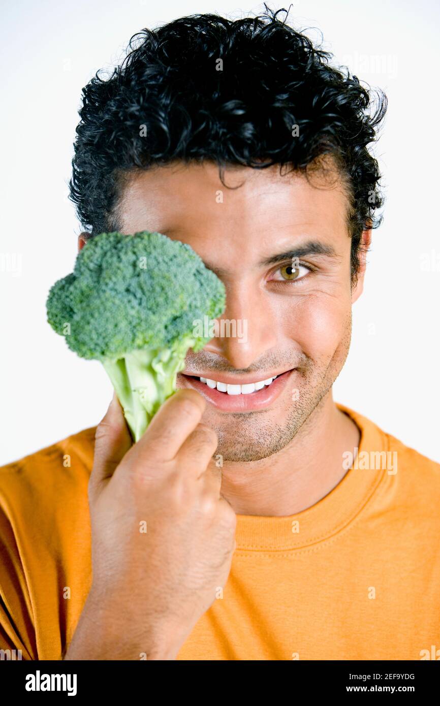 Portrait of a young man holding a broccoli in front of his face and ...