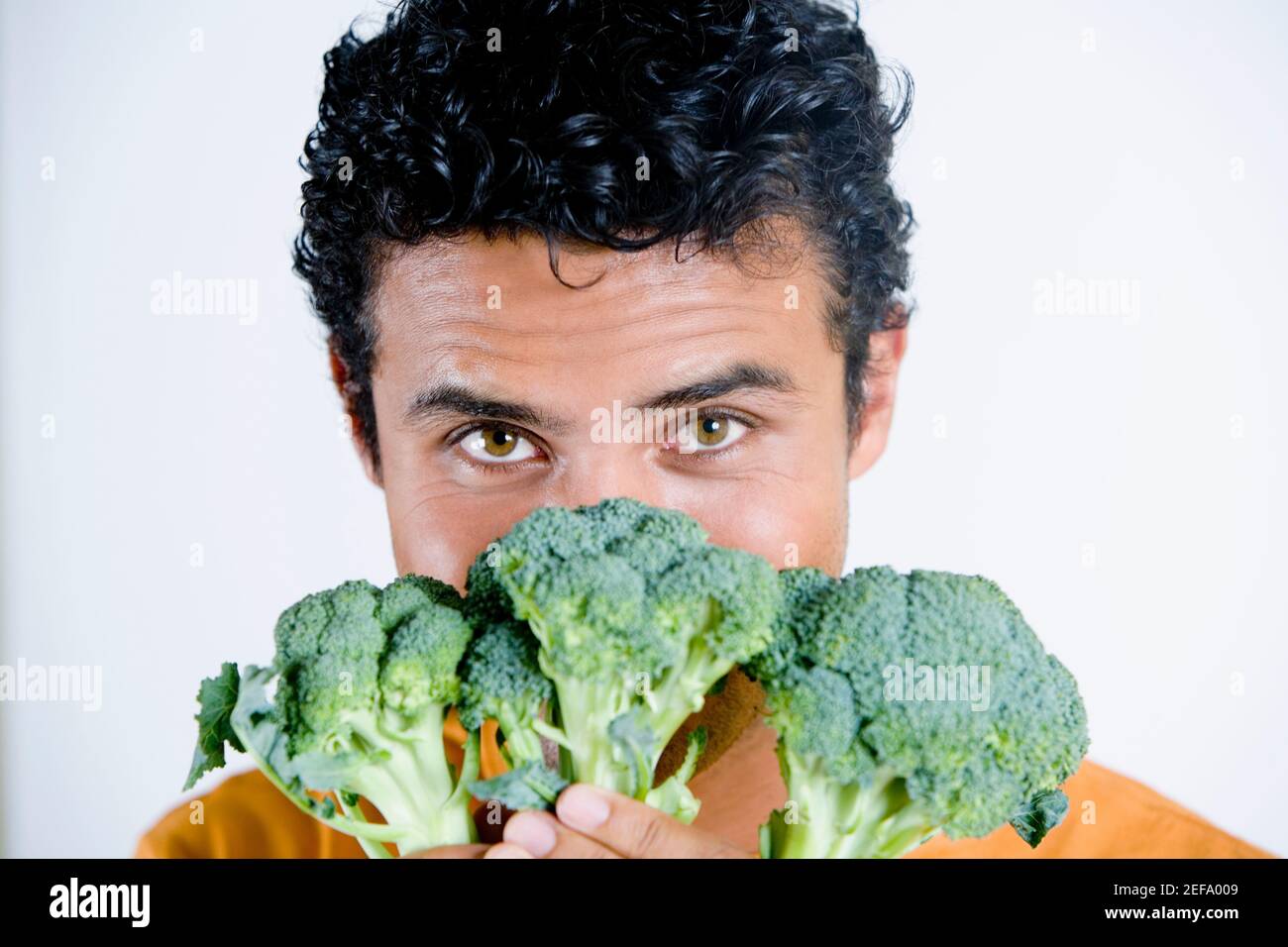 Portrait of a young man holding broccoli in front of his face Stock ...