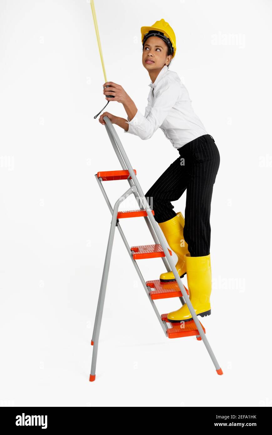 Side profile of a female architect climbing a ladder and holding a tape ...