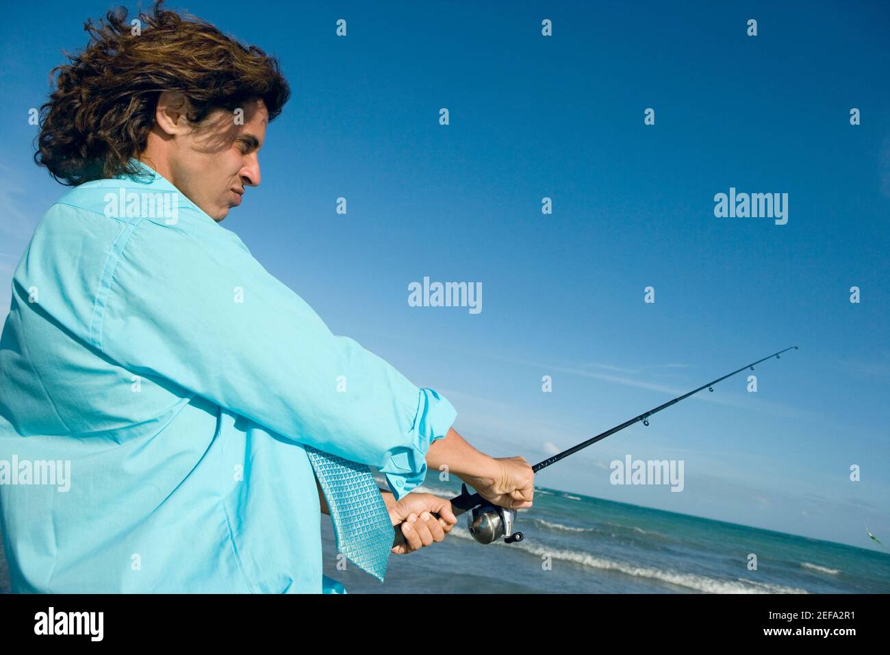 Side profile of a mid adult man holding a fishing rod on the beach ...