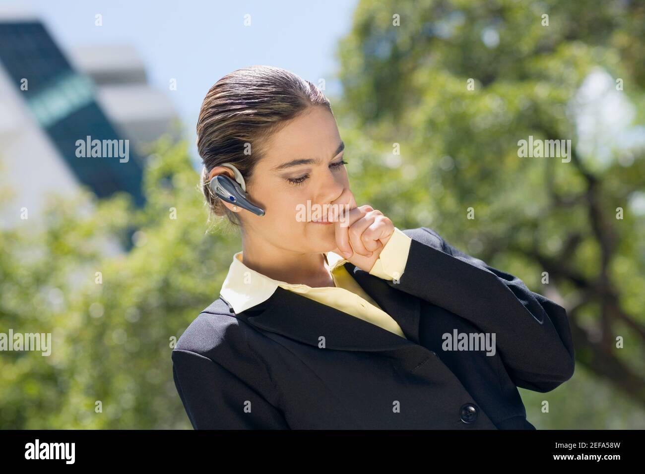 Businesswoman wearing a bluetooth device with her hands covering her ...