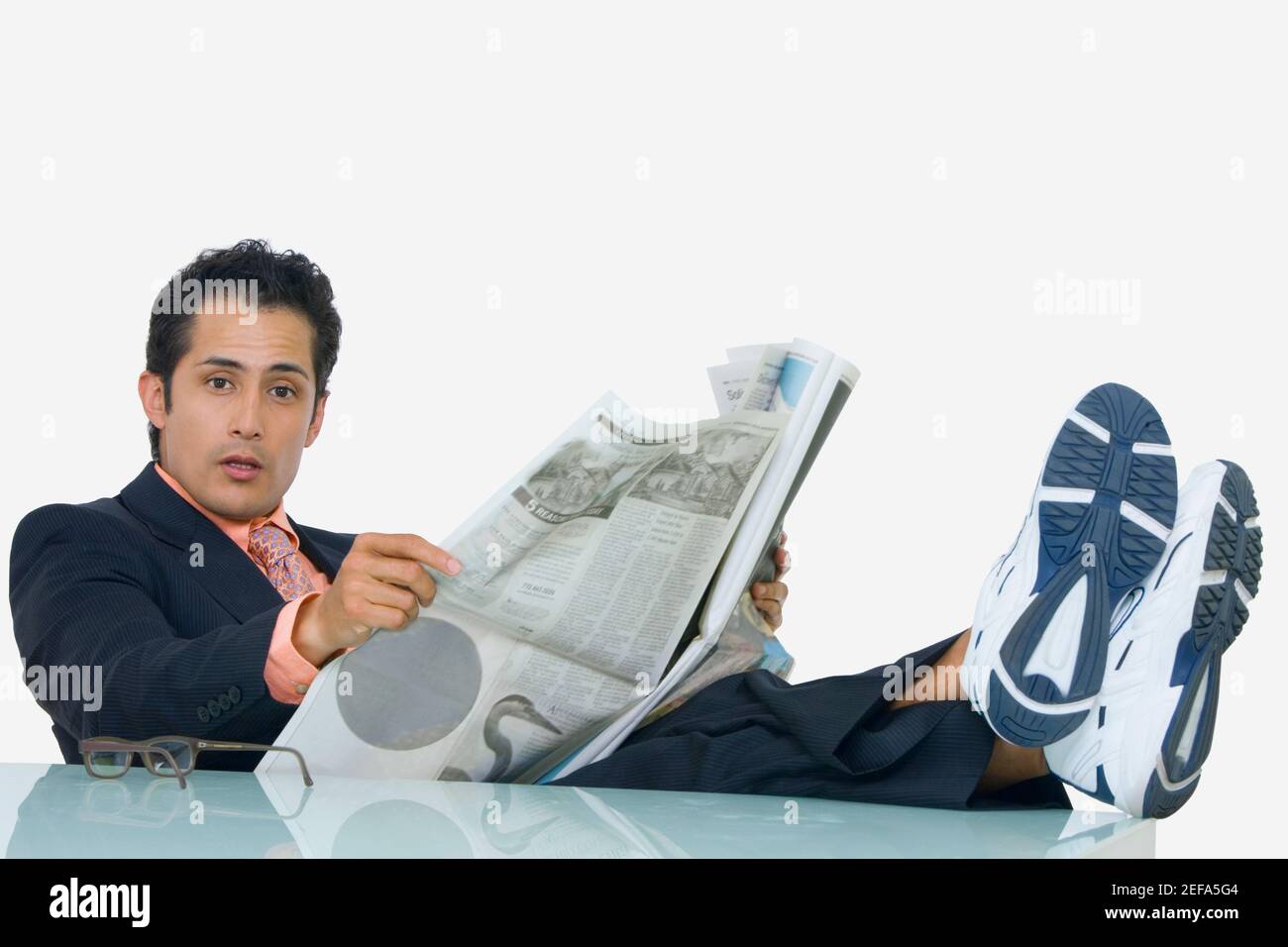 Portrait of a businessman resting his legs on the table and reading a ...