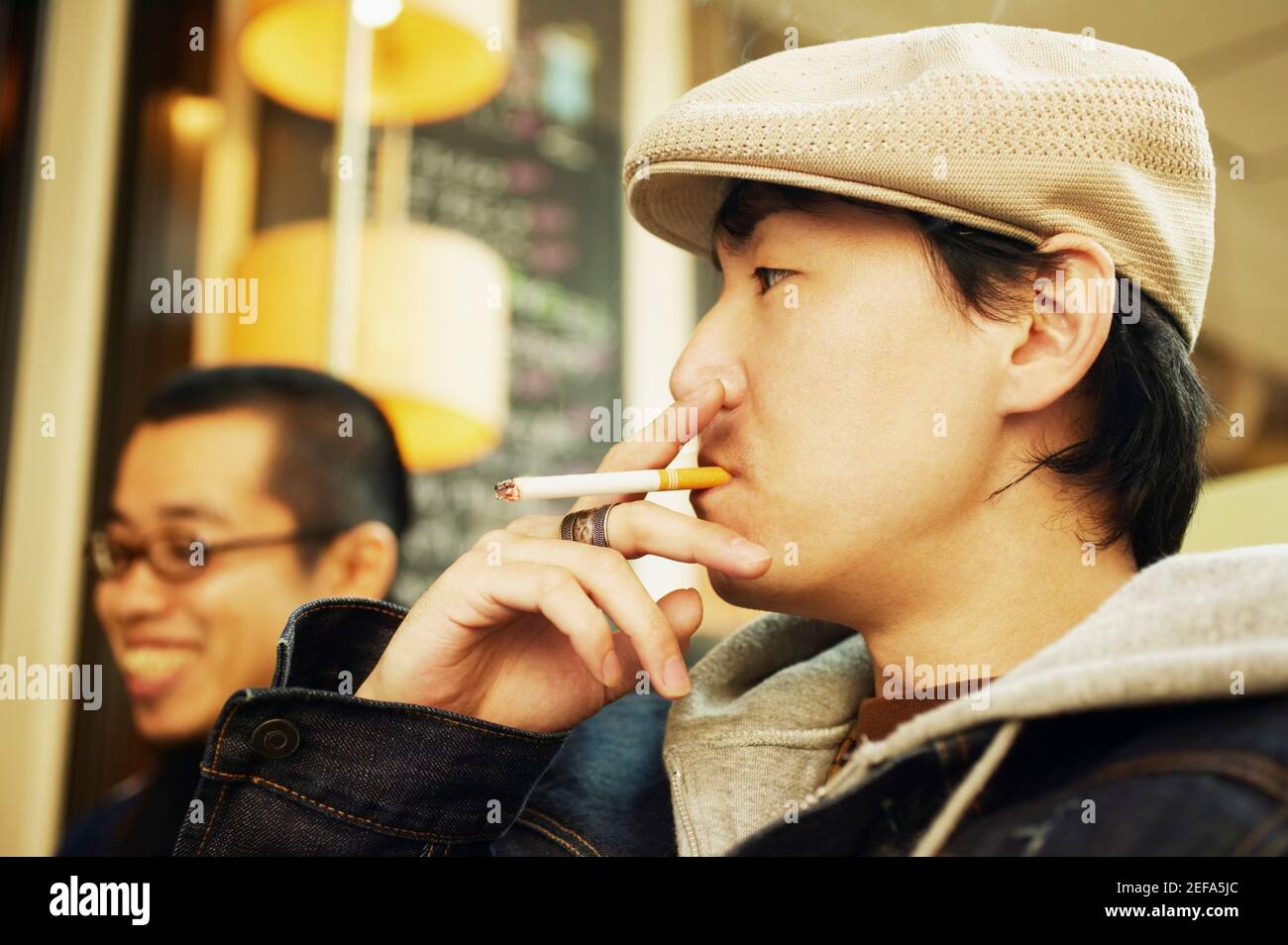 Side profile of a mid adult man smoking a cigarette and a young man ...