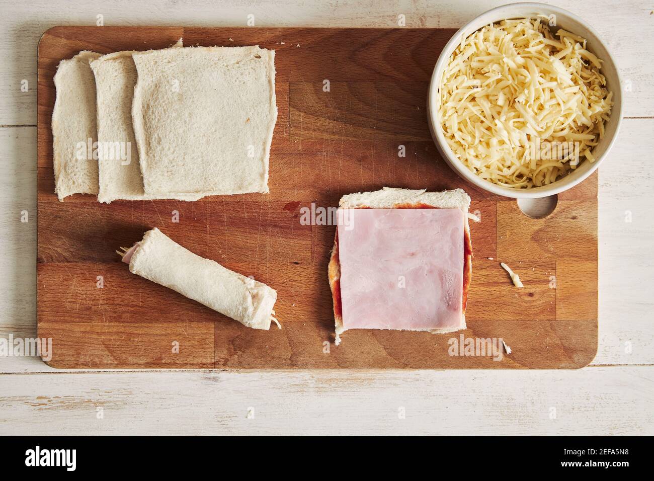 Top view of raw toast rolls with ham and grated cheese on a board on ...