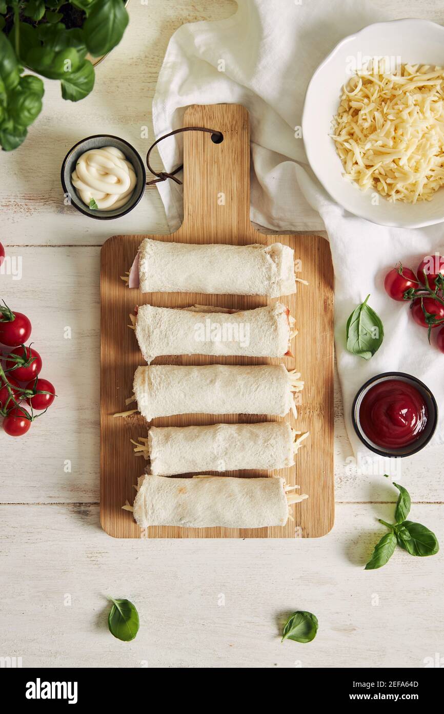 Top view of raw ham and cheese toast rolls on a board on the table with ...