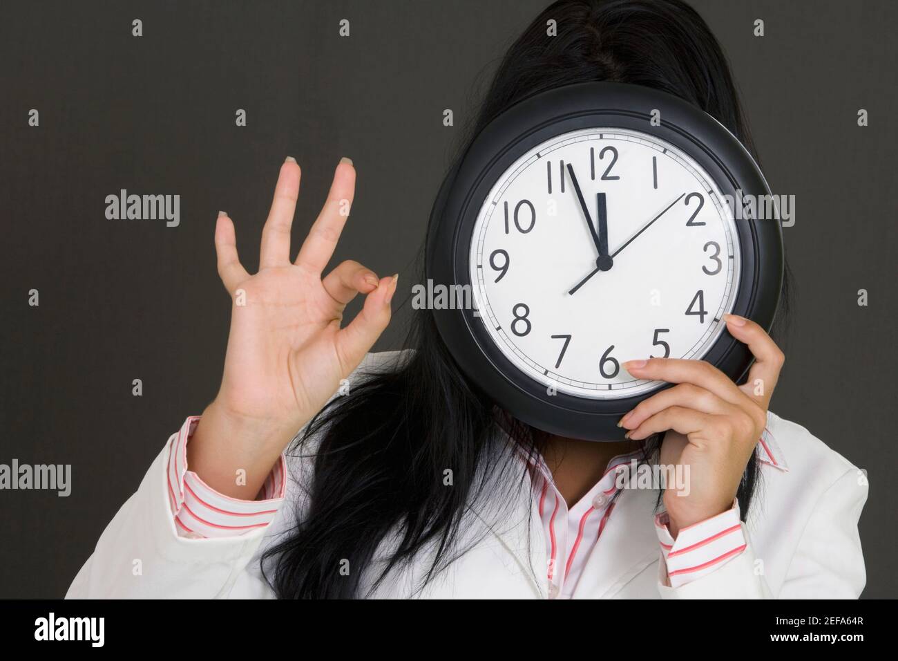Close-up of a businesswoman holding a clock in front of her face and ...