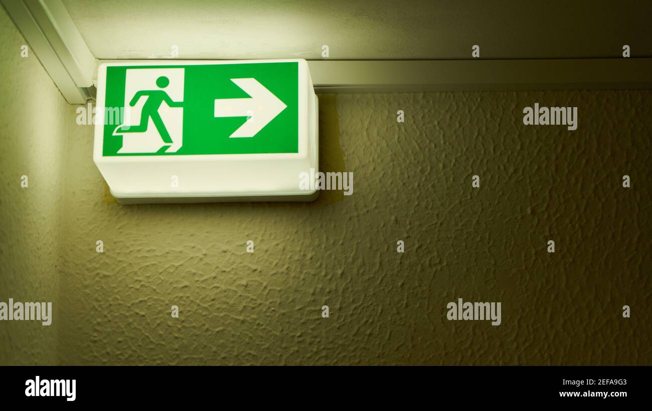Green glowing emergency exit sign on wall in the house as a notice sign ...