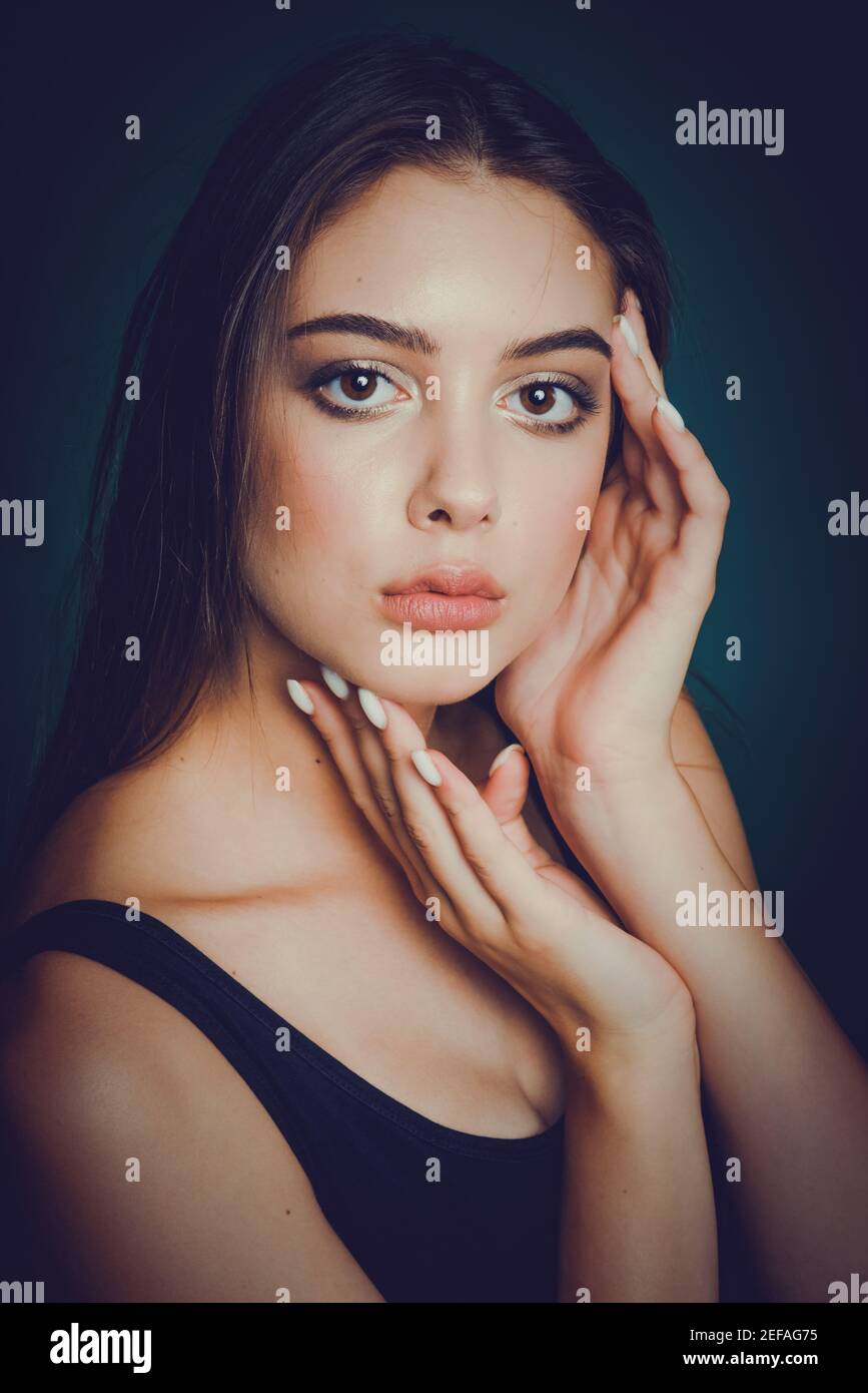 portrait of a young and beautiful woman with her hands near face ...