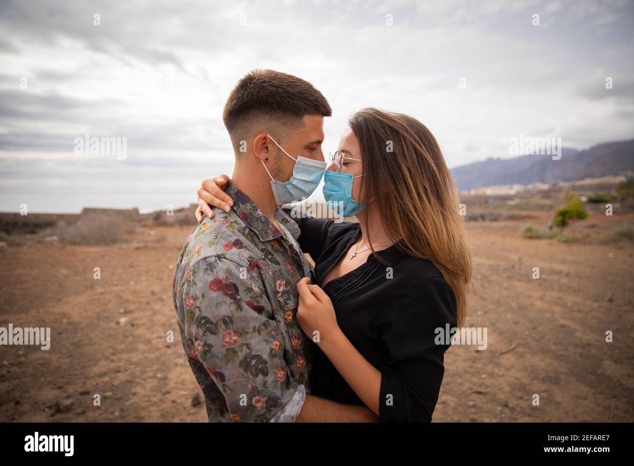 Couple wear surgical masks, during a moment of cuddles, to stay safe ...