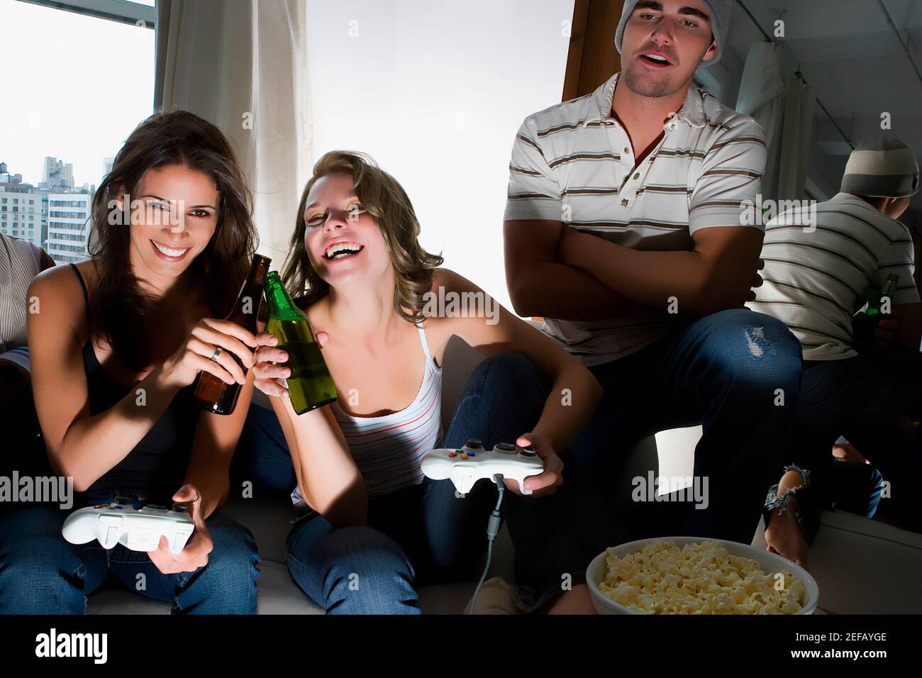 Two young women toasting with beer bottles and a young man standing ...