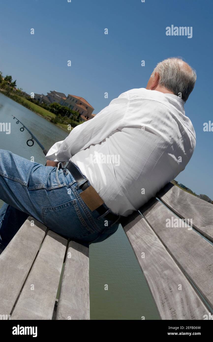 Rear view of a senior man sitting on a bench at the lakeside and ...