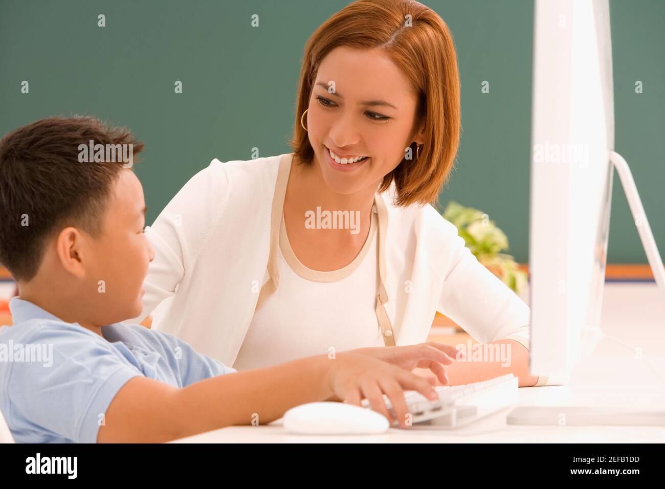 Side profile of a schoolboy with his teacher in front of a computer and ...