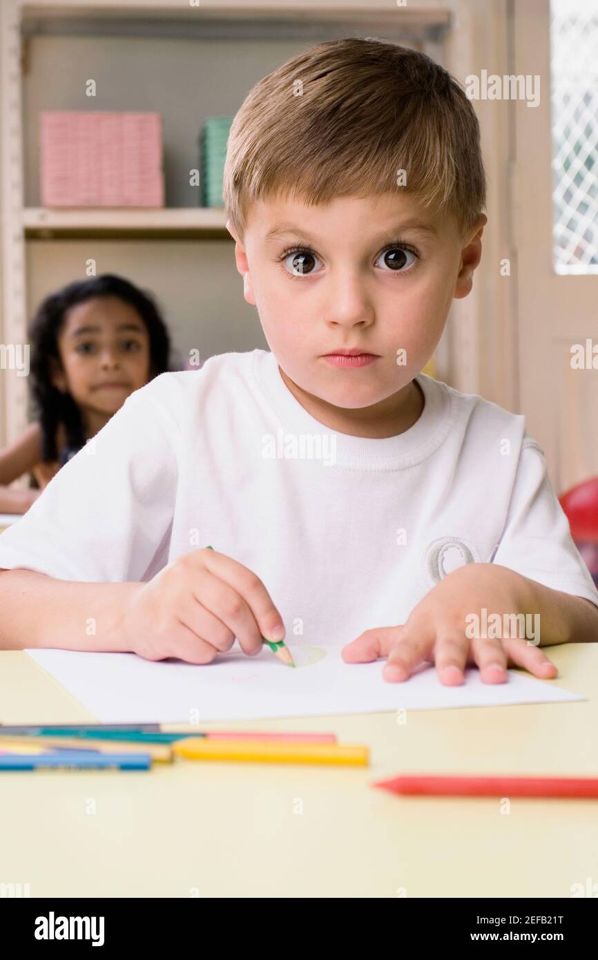 Portrait of a boy drawing on a sheet of paper with a girl sitting ...