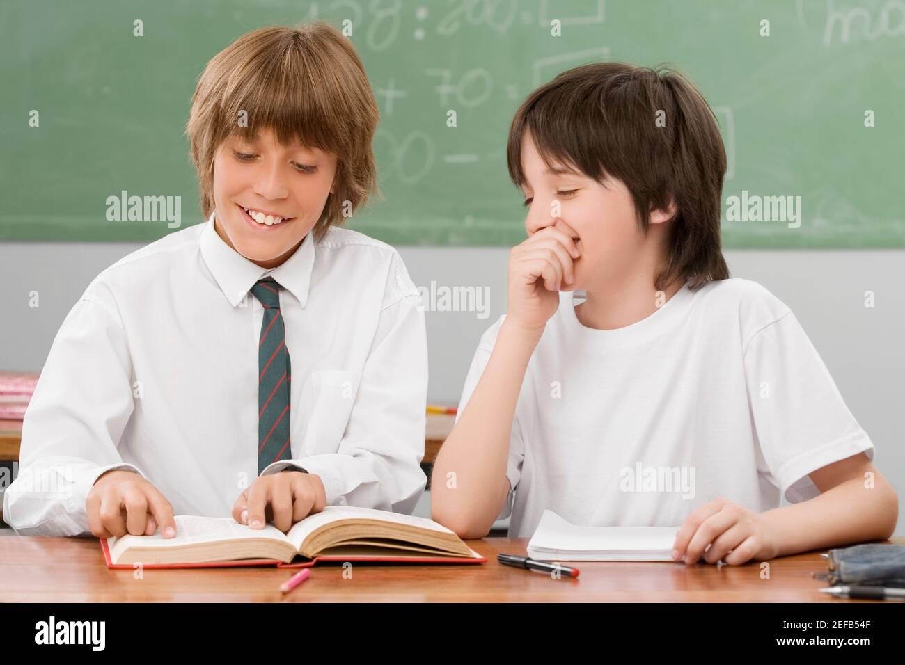 Two schoolboys reading a book together in a classroom and smiling Stock ...