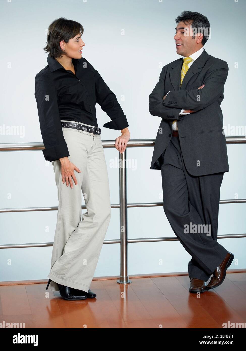 Businessman and a businesswoman leaning against a railing and talking ...