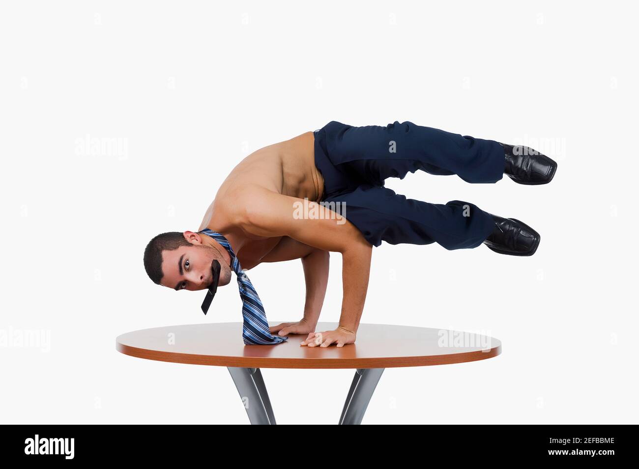 Portrait of a businessman doing a handstand on a table with a mobile ...