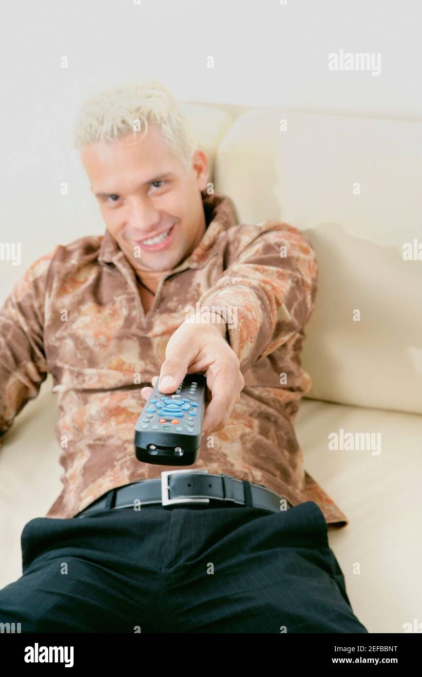 Young man sitting on a couch and operating a remote control Stock Photo ...