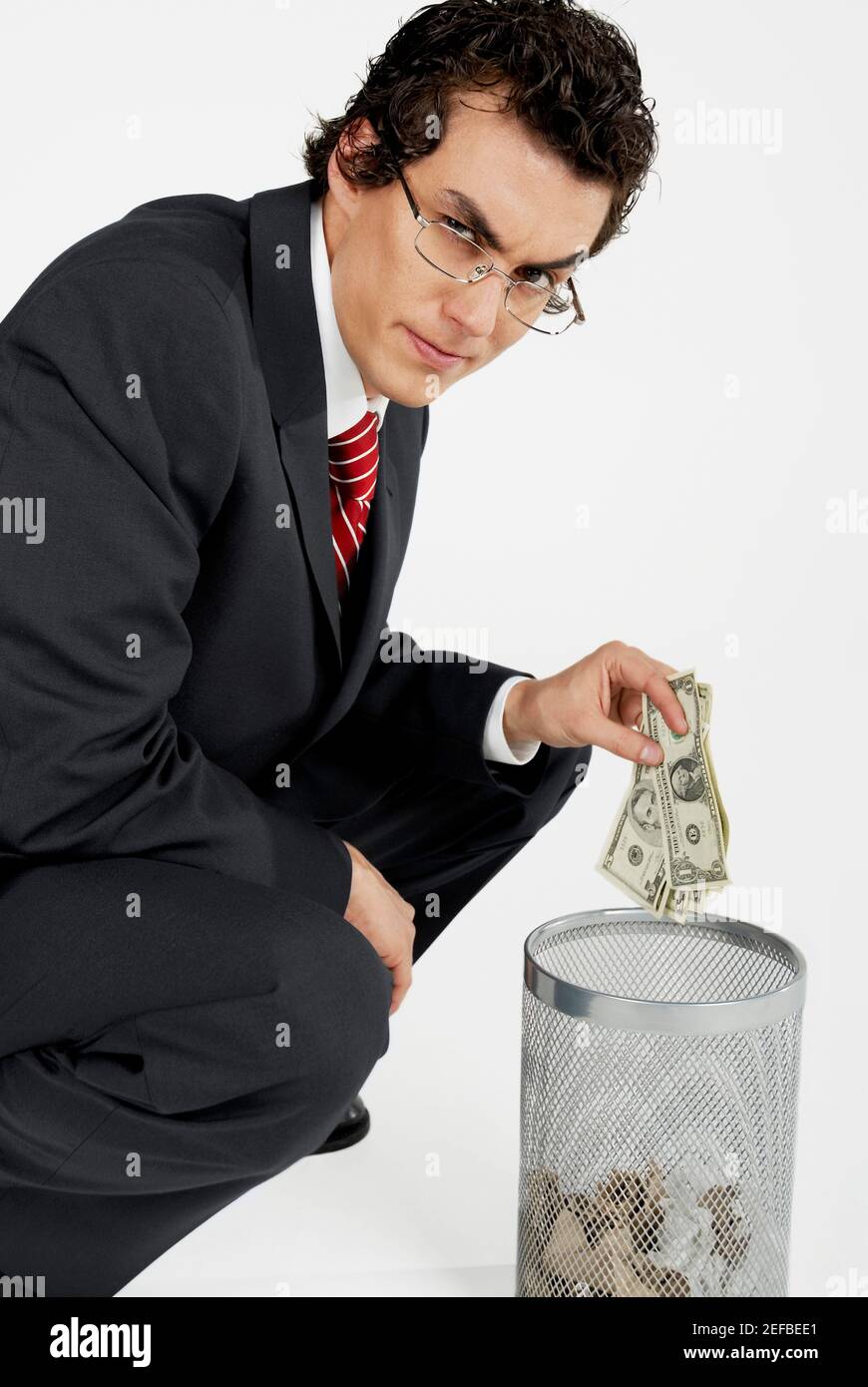 Portrait of a businessman throwing paper currency into a wastepaper ...