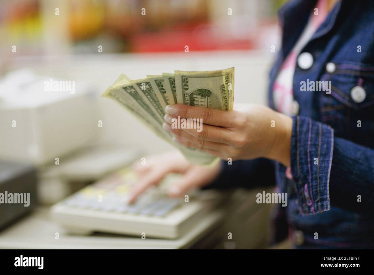 Mid section view of a sales clerk holding paper currency in a checkout ...