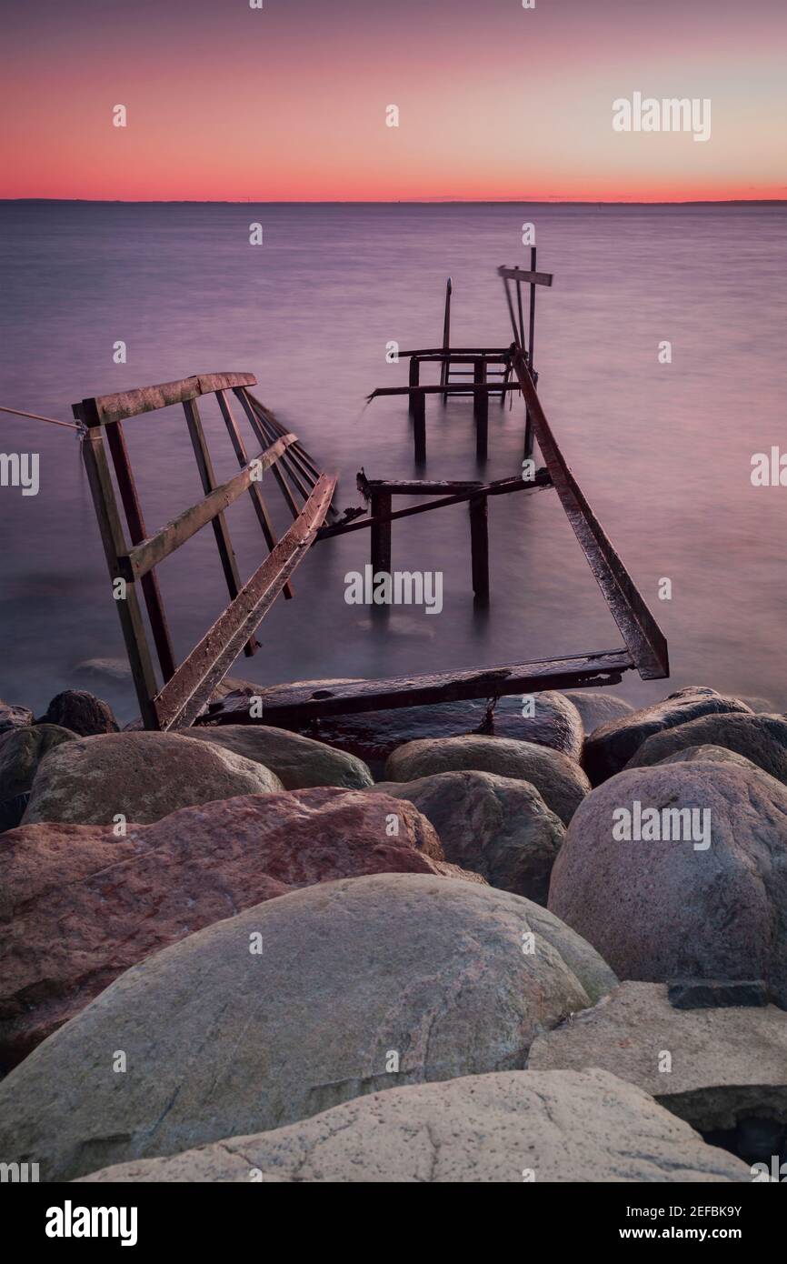Old wooden jetty falling into the sea during lovely gradient sunset ...