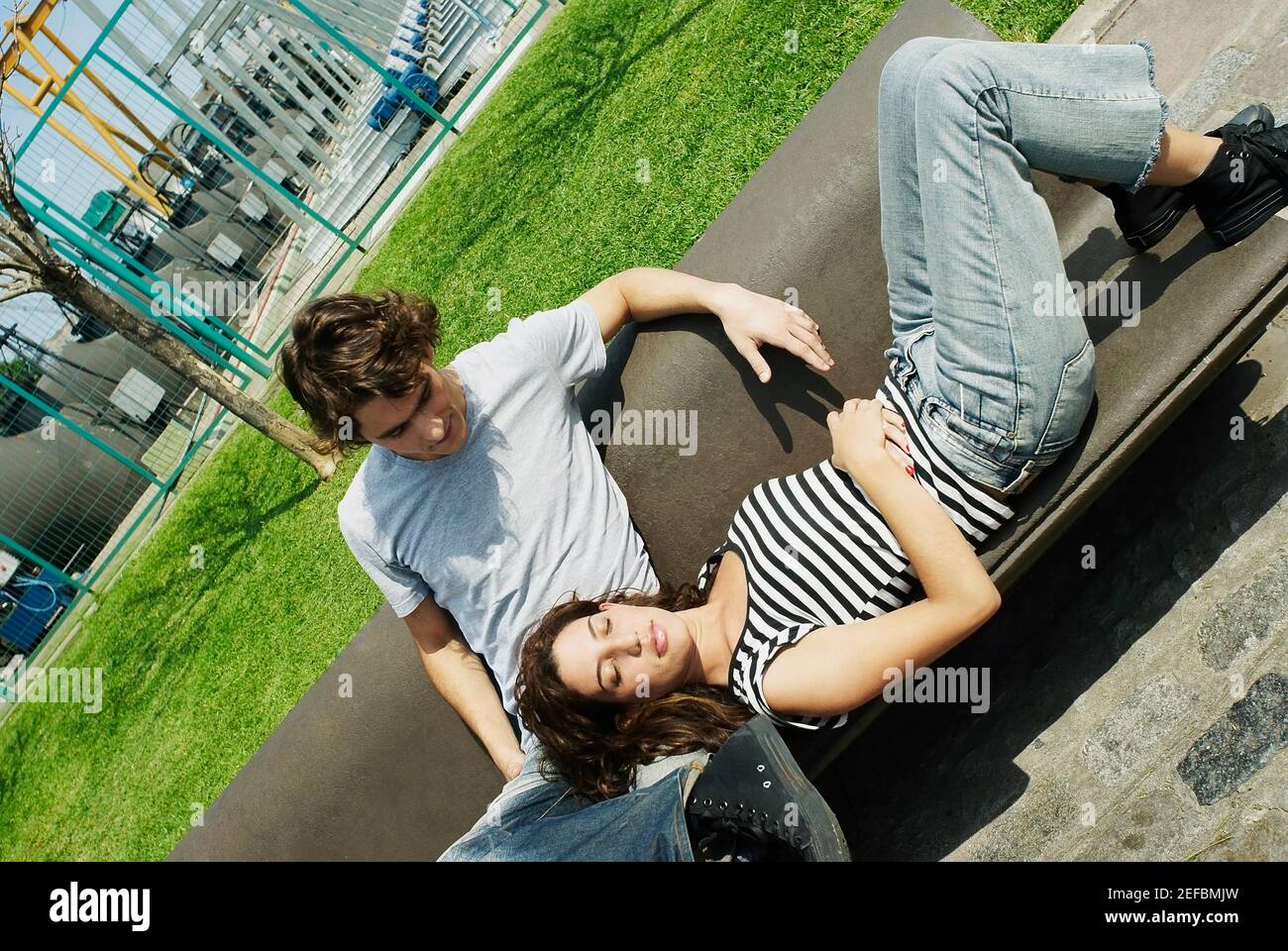 Young woman lying on a bench resting her head in the lap of a young man ...