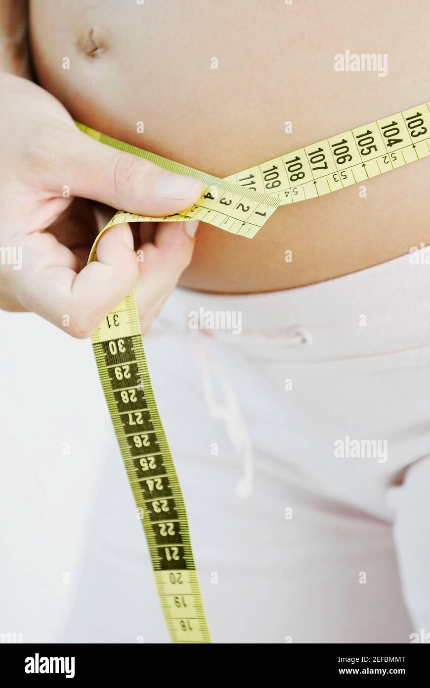 Mid section view of a pregnant woman measuring her abdomen with a tape ...