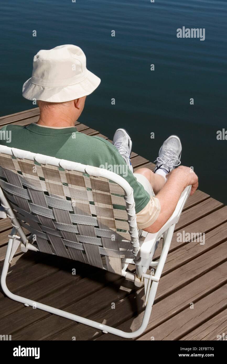 Rear view of a senior man sitting on a chair at the lakeside Stock ...