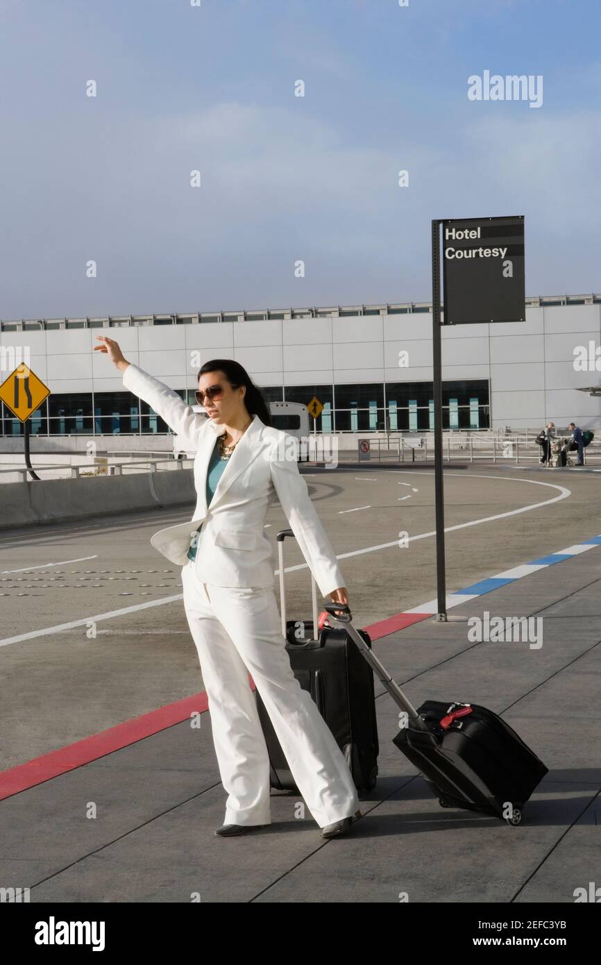 Businesswoman hailing a taxi outside an airport Stock Photo - Alamy