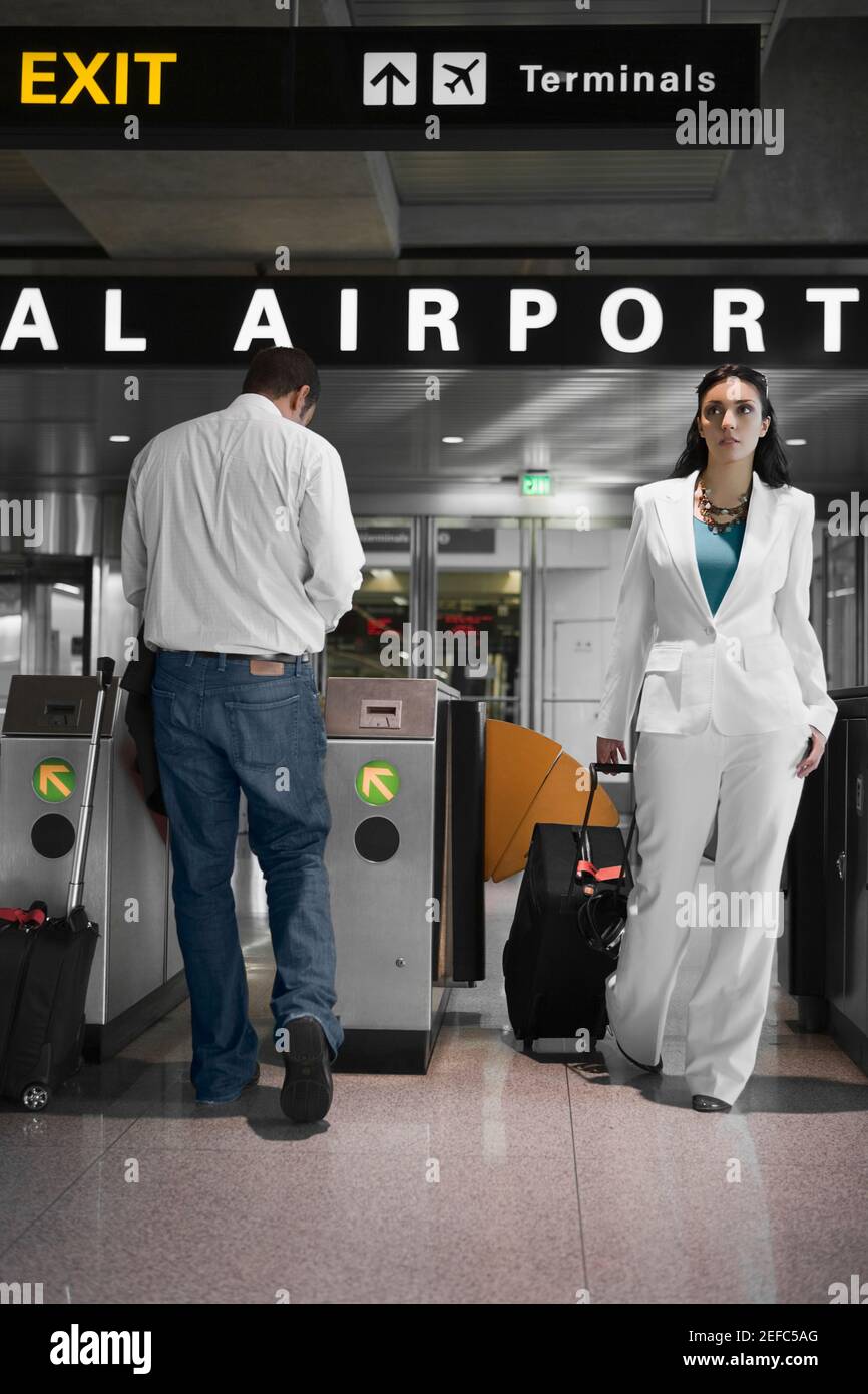 Businesswoman pulling her luggage and a mid adult man standing near a ...