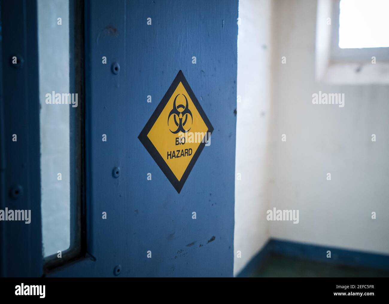 Warning danger biohazard sticker on prison cell blue open door sunlight ...