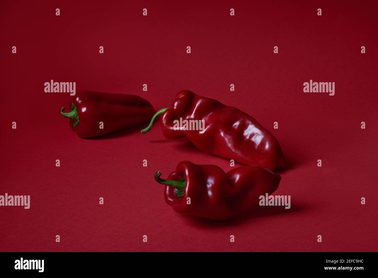 Three red peppers on a red background Stock Photo - Alamy