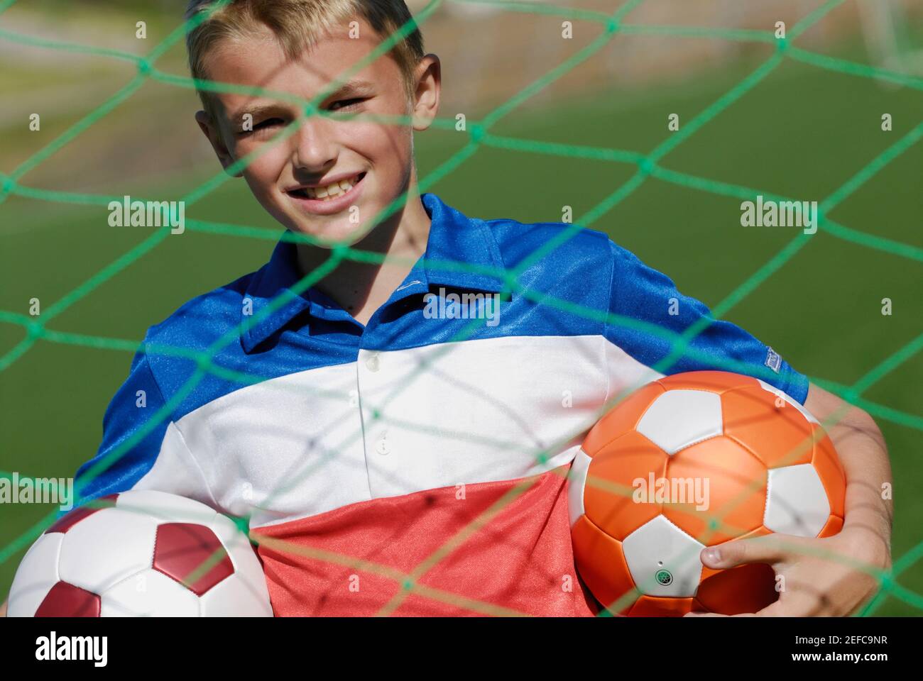 Portrait of a soccer player standing behind the net and holding two ...